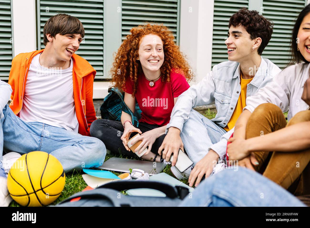Teenage school students laughing together sitting on grass at campus ...
