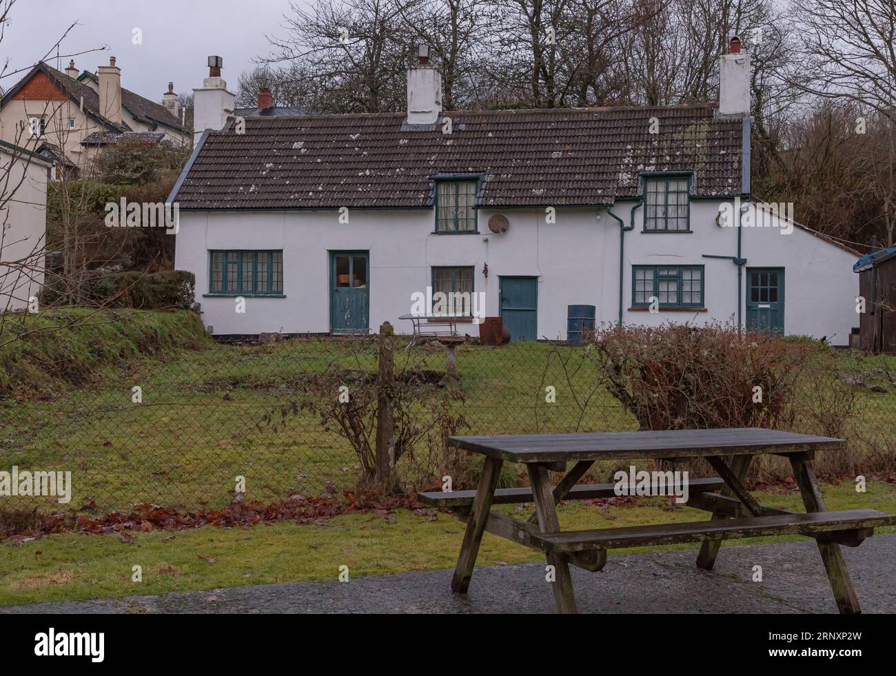 White painted cottage in the winter behind a fence and picnic bench ...