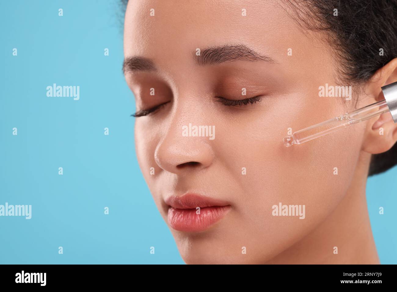 Beautiful woman applying serum onto her face on light blue background ...