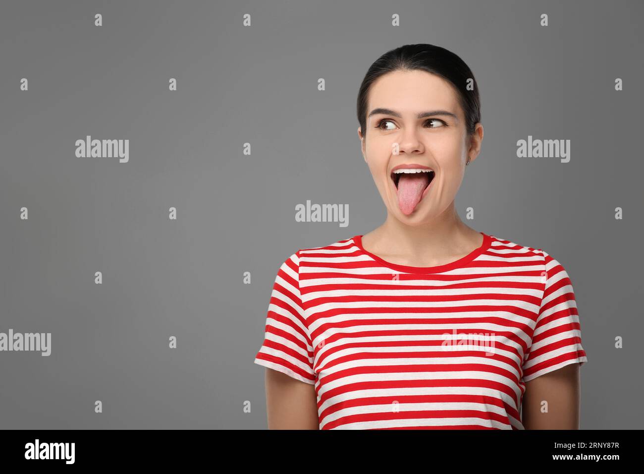 Happy young woman showing her tongue on grey background. Space for text ...