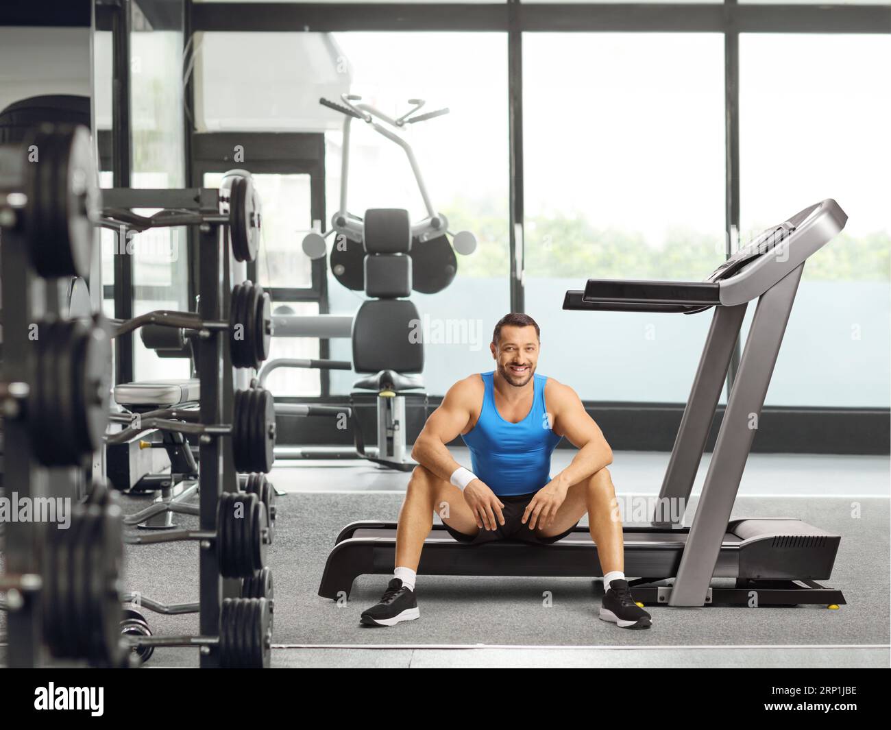 Smiling young man sitting on a treadmill at a gym Stock Photo - Alamy