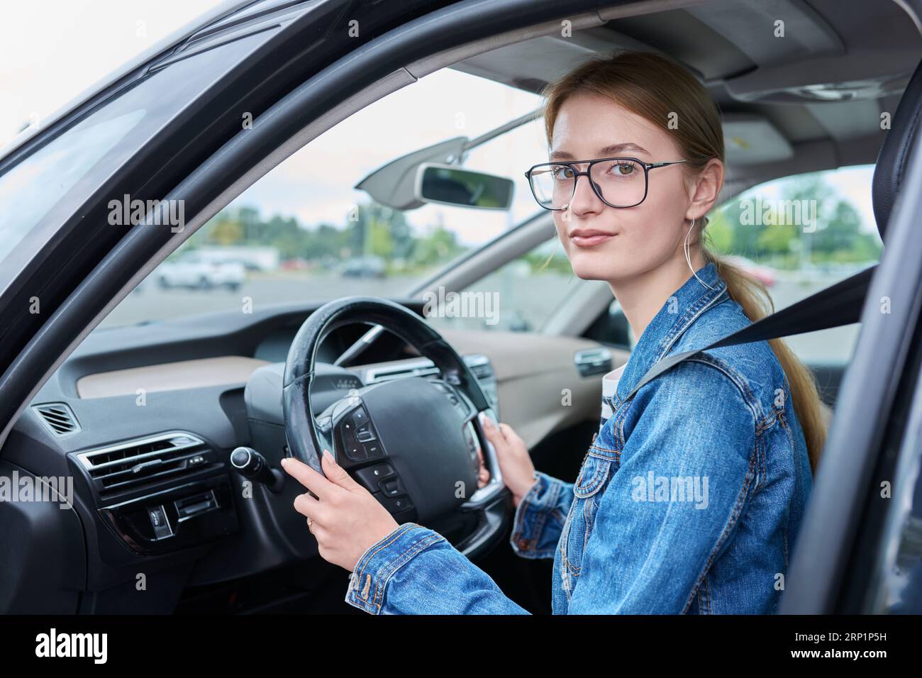 Teenage girl driver in glasses sitting behind wheel of car, looking at ...
