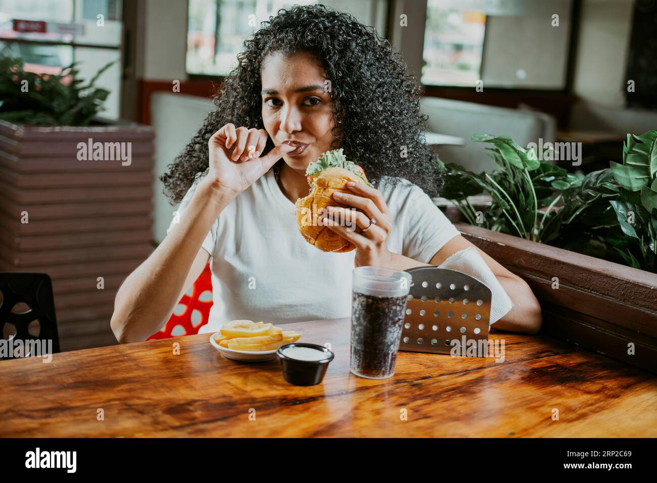 Latin Woman Sucking Her Fingers Holding A Hamburger In A Restaurant