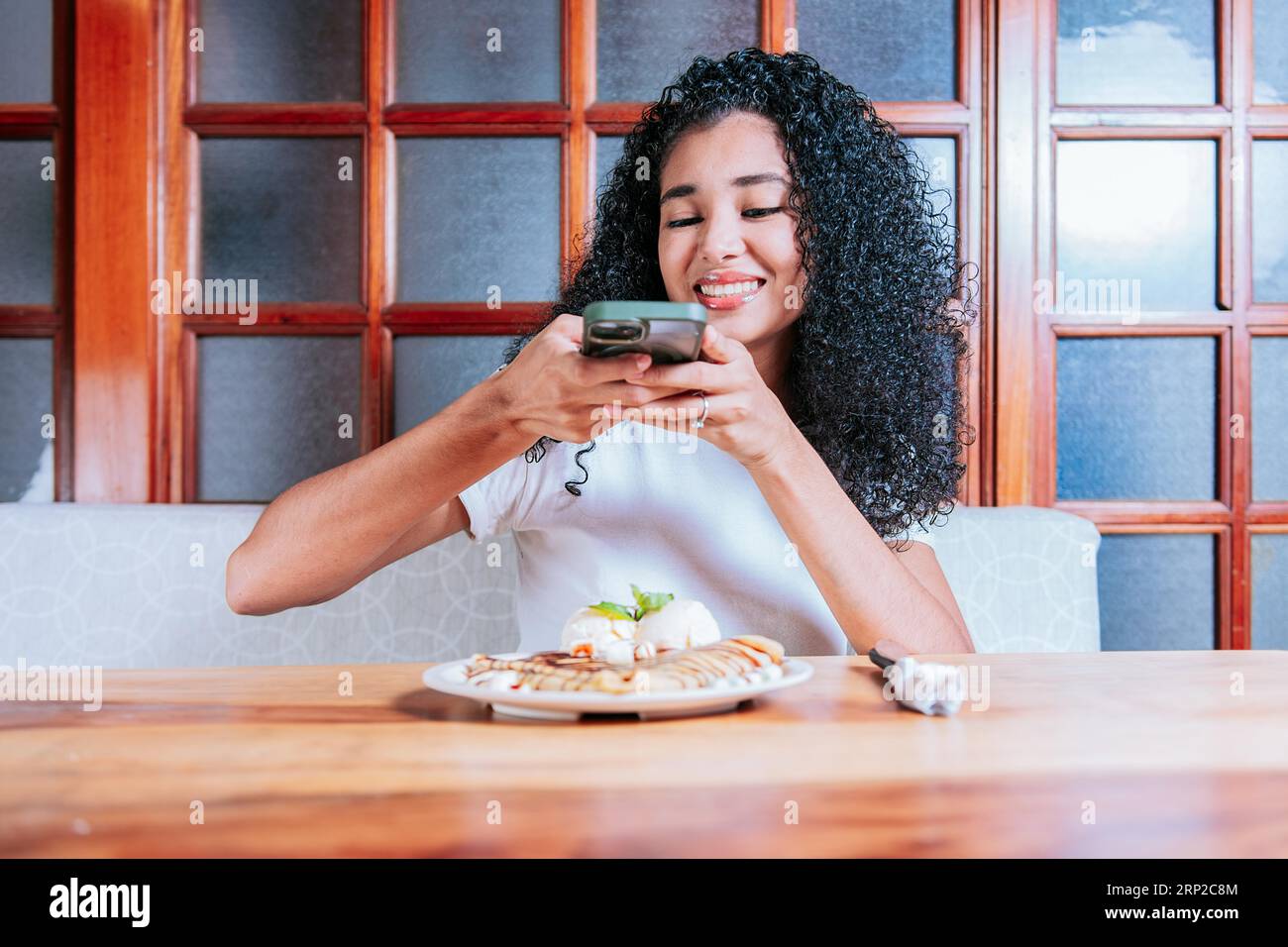 Young woman using cell phone and taking a picture of chocolate crepe ...