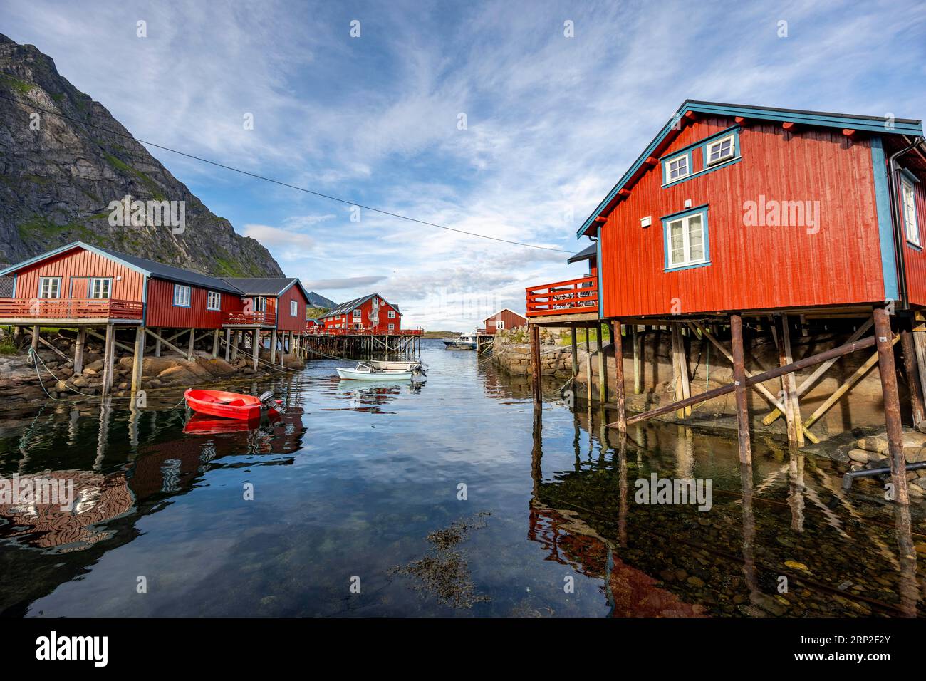 Traditional red rorbuer wooden huts, on stilts on the shore, reflected ...