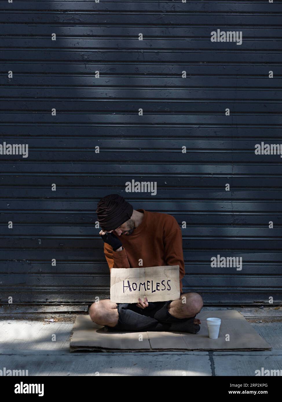 Homeless man hiding his face asking money long view Stock Photo - Alamy