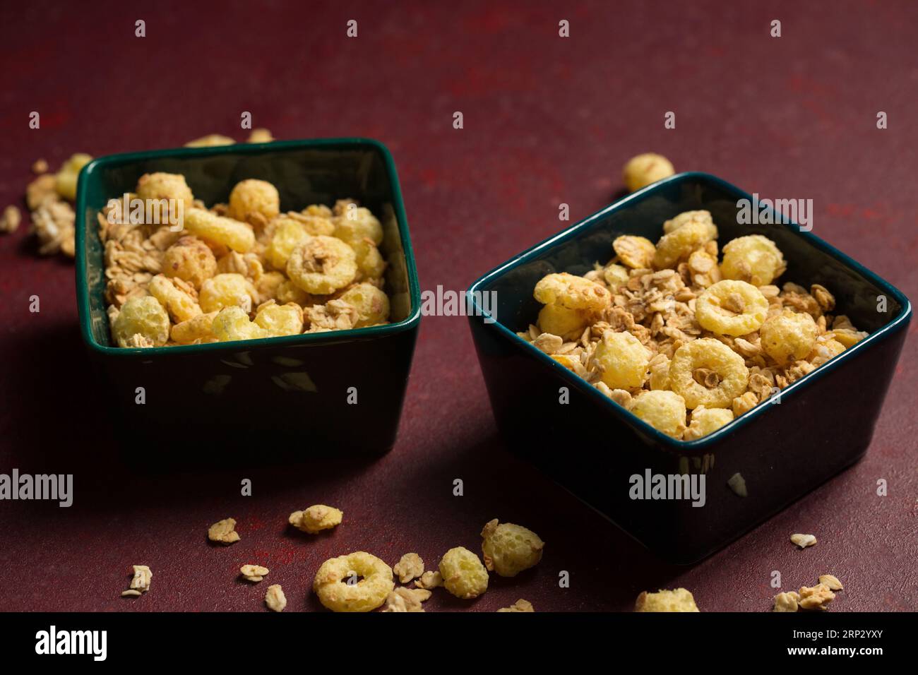 Breakfast cereal with granola and corn rings in small bowls on maroon ...