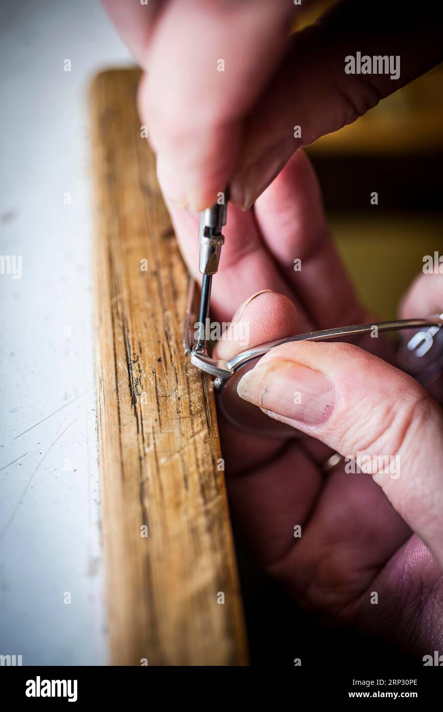 An optician adjusts a temple of a pair of glasses with a screwdriver ...