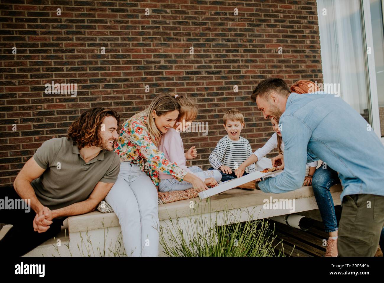 Happy group of young people and kids eating pizza in the house backyard ...