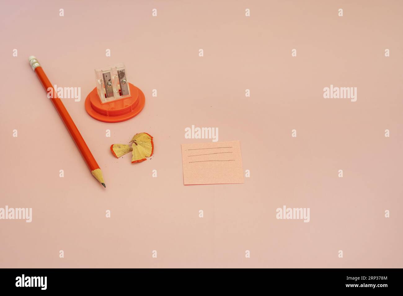 A sharpened orange pencil with a small eraser on one end next to a ...