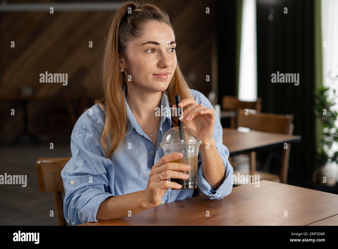 Young woman drinking bubble tea in a cafe looks away thinking Stock Photo - Alamy