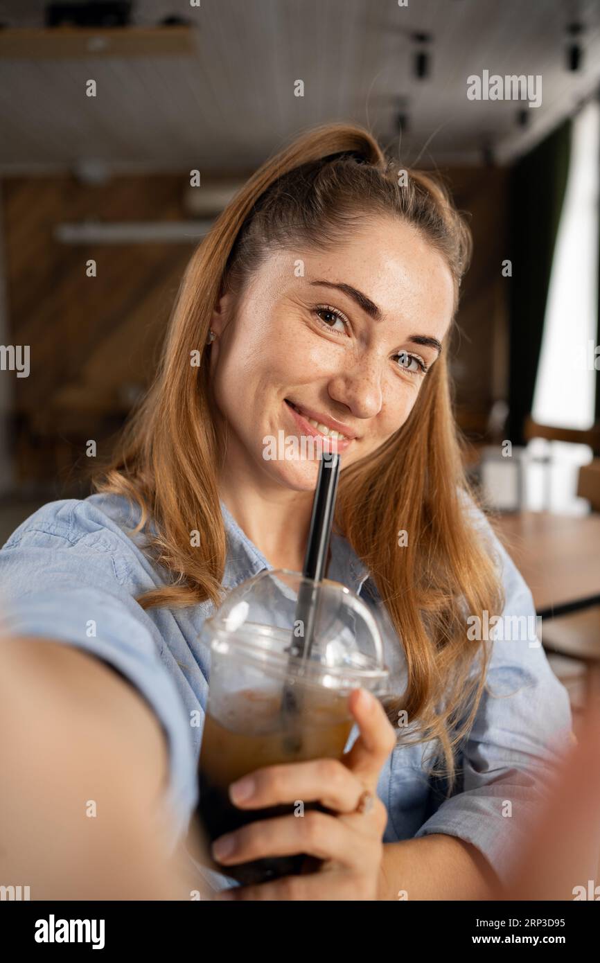 Woman taking a selfie with bubble tea sitting in a cafe, close-up of a ...