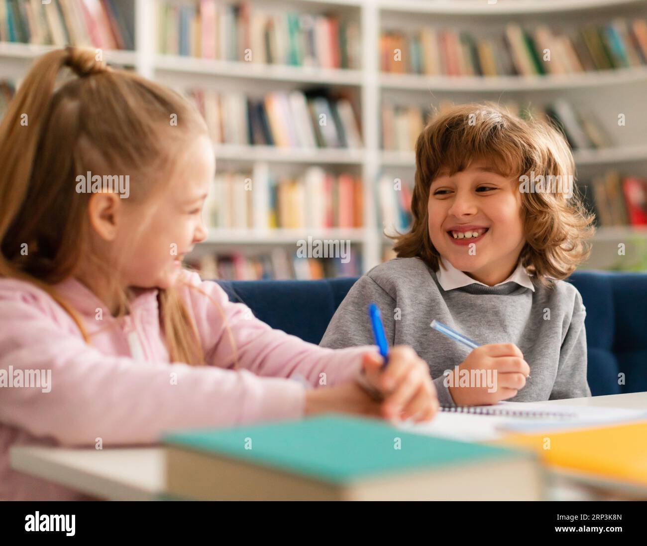 Happy schoolchildren friends sitting at table in classroom at primary ...