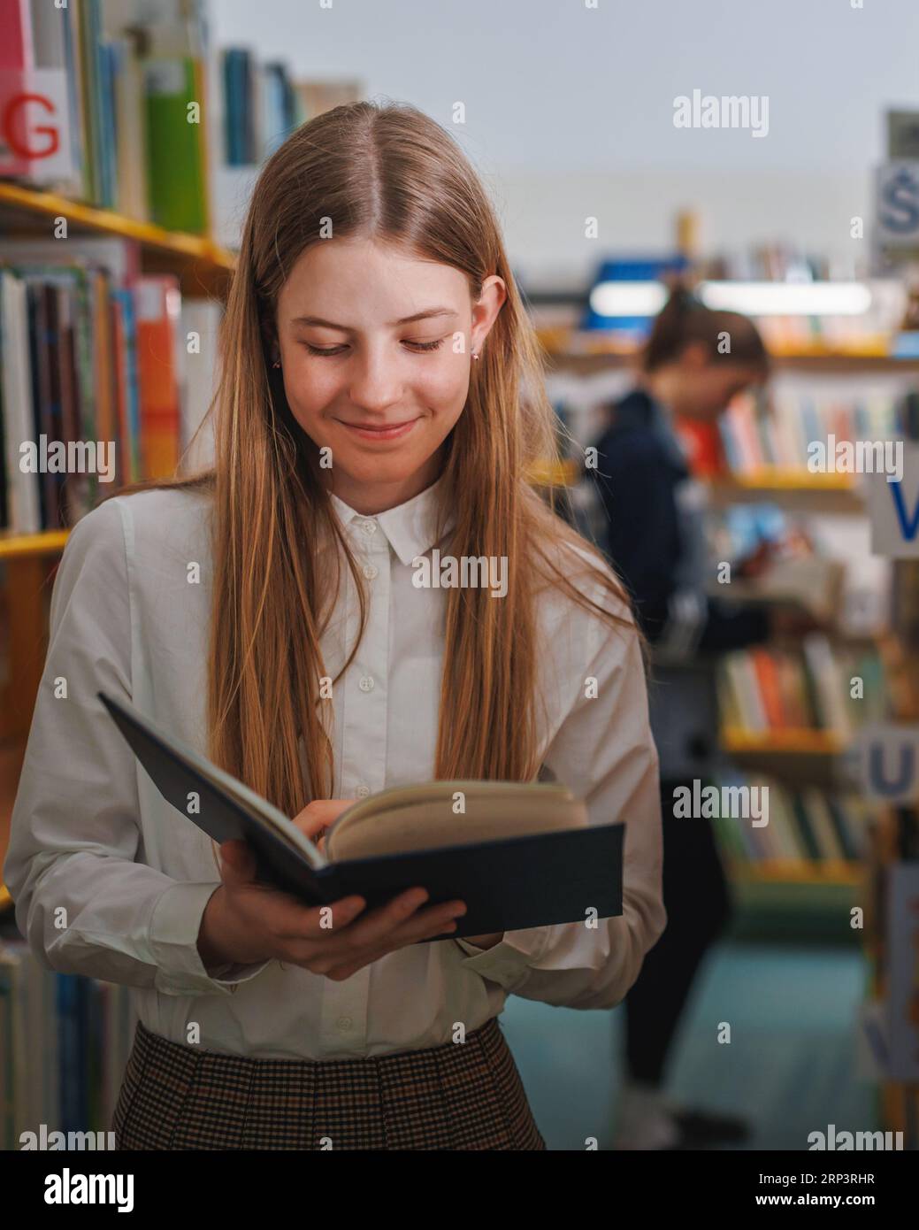 Teenage girl taking a book from a bookshelf in the school library ...