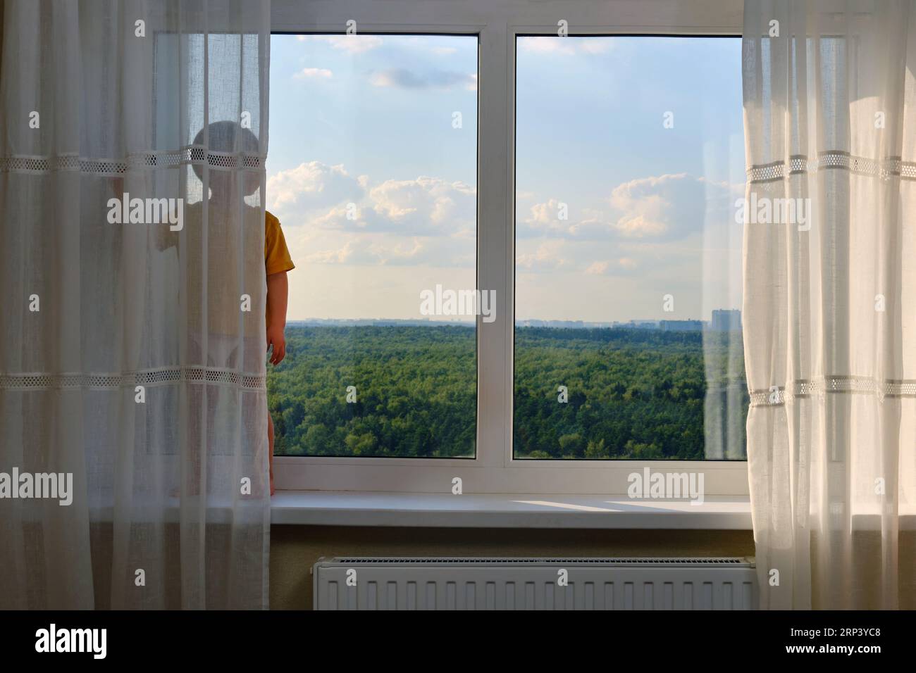 The little child is standing on the window sill, gazing out at the sky ...