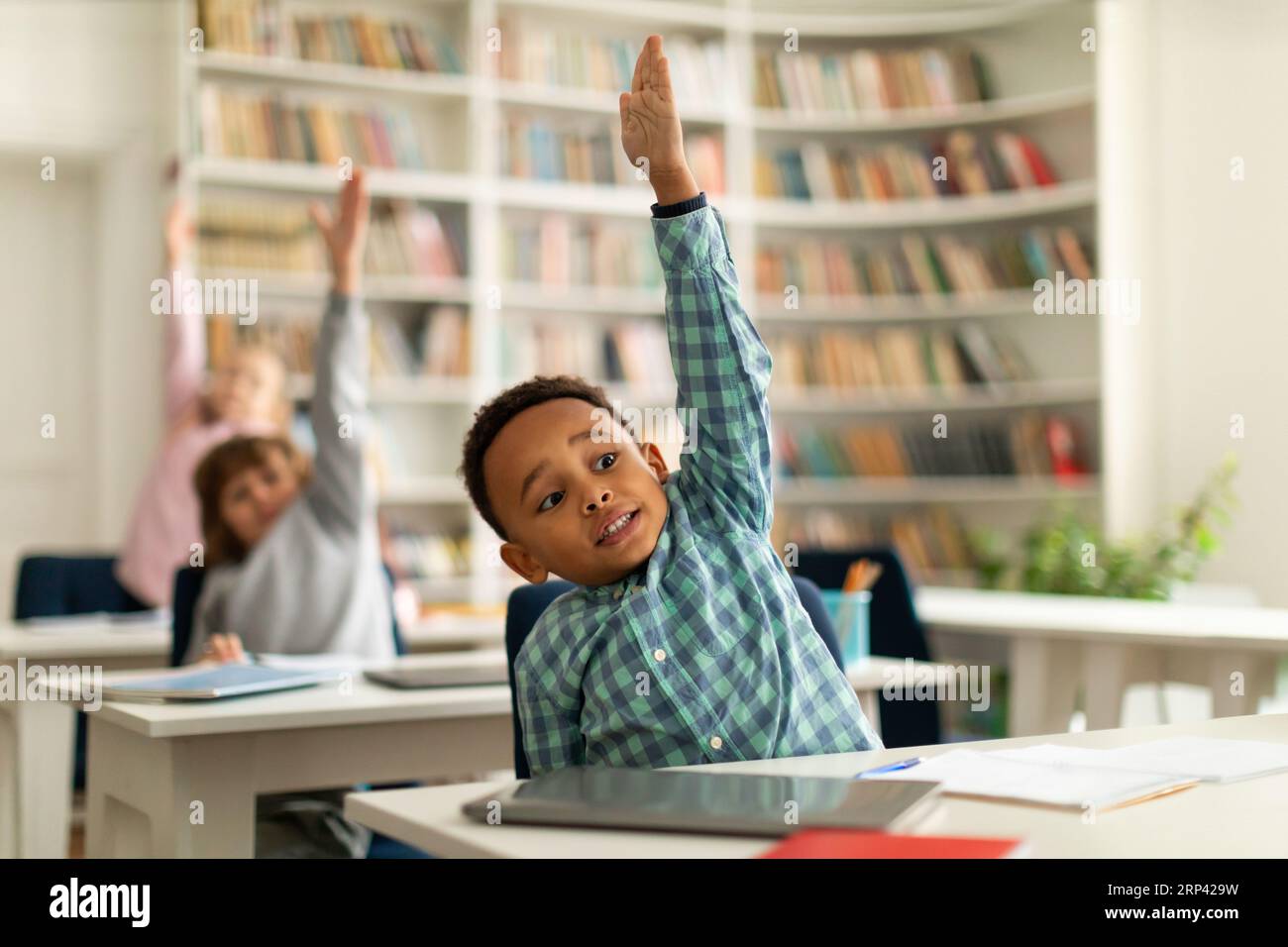 Diverse elementary school students raising hands to answer teacher ...