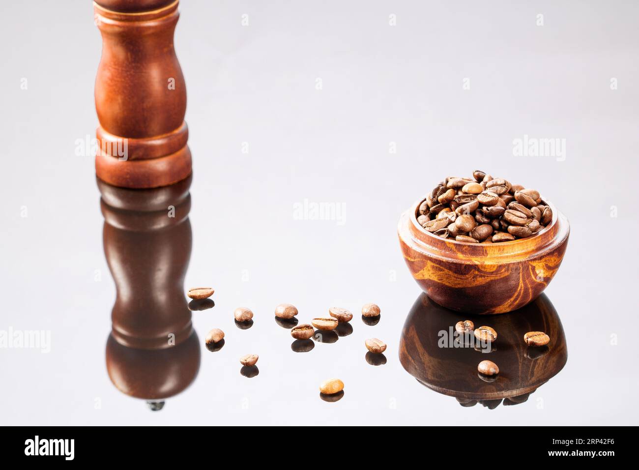 A wooden cup filled with coffee beans is reflected in a black mirror ...