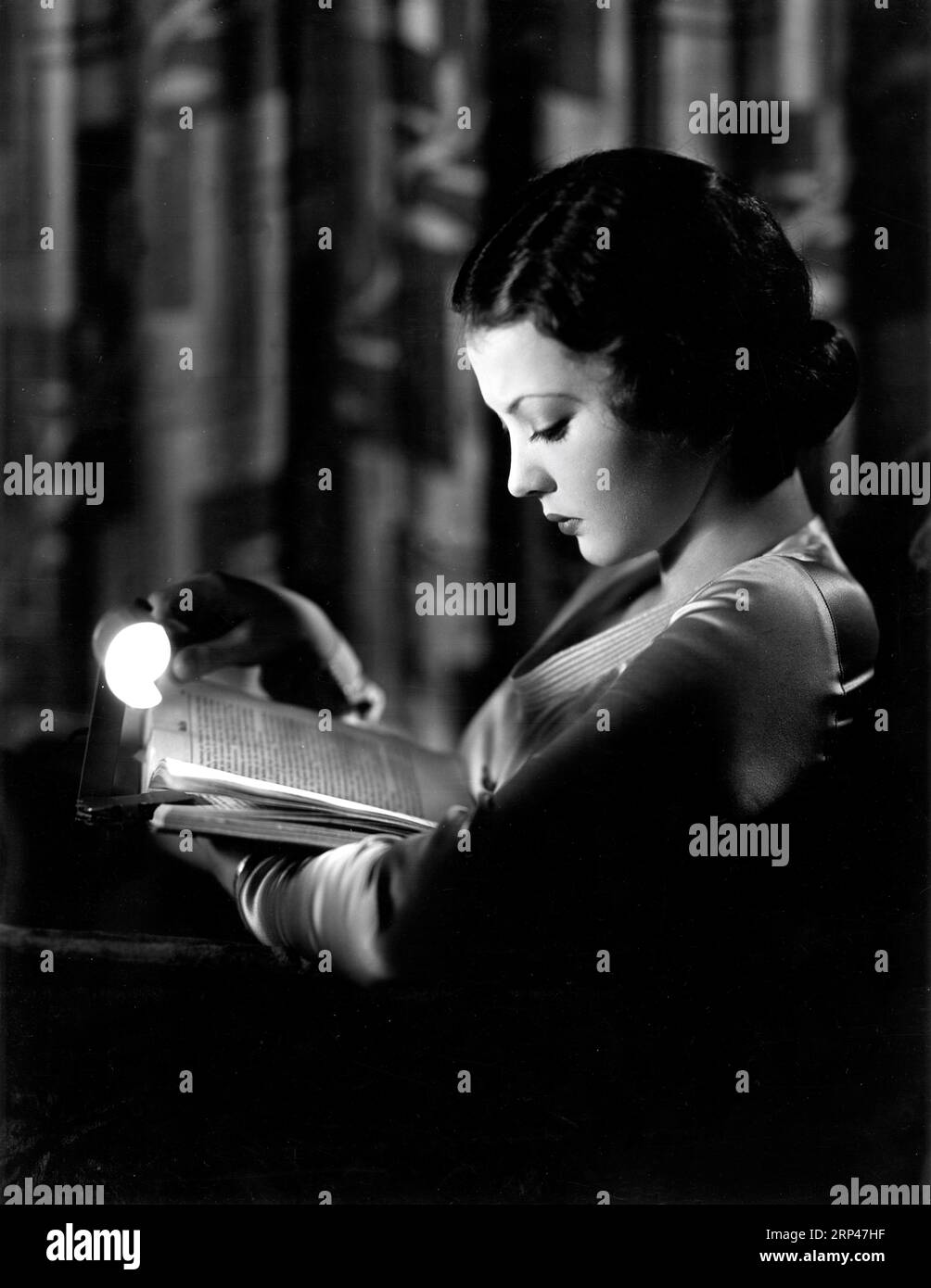 SYLVIA SIDNEY on set candid reading a book using a booklight during a break in filming of PICK ...