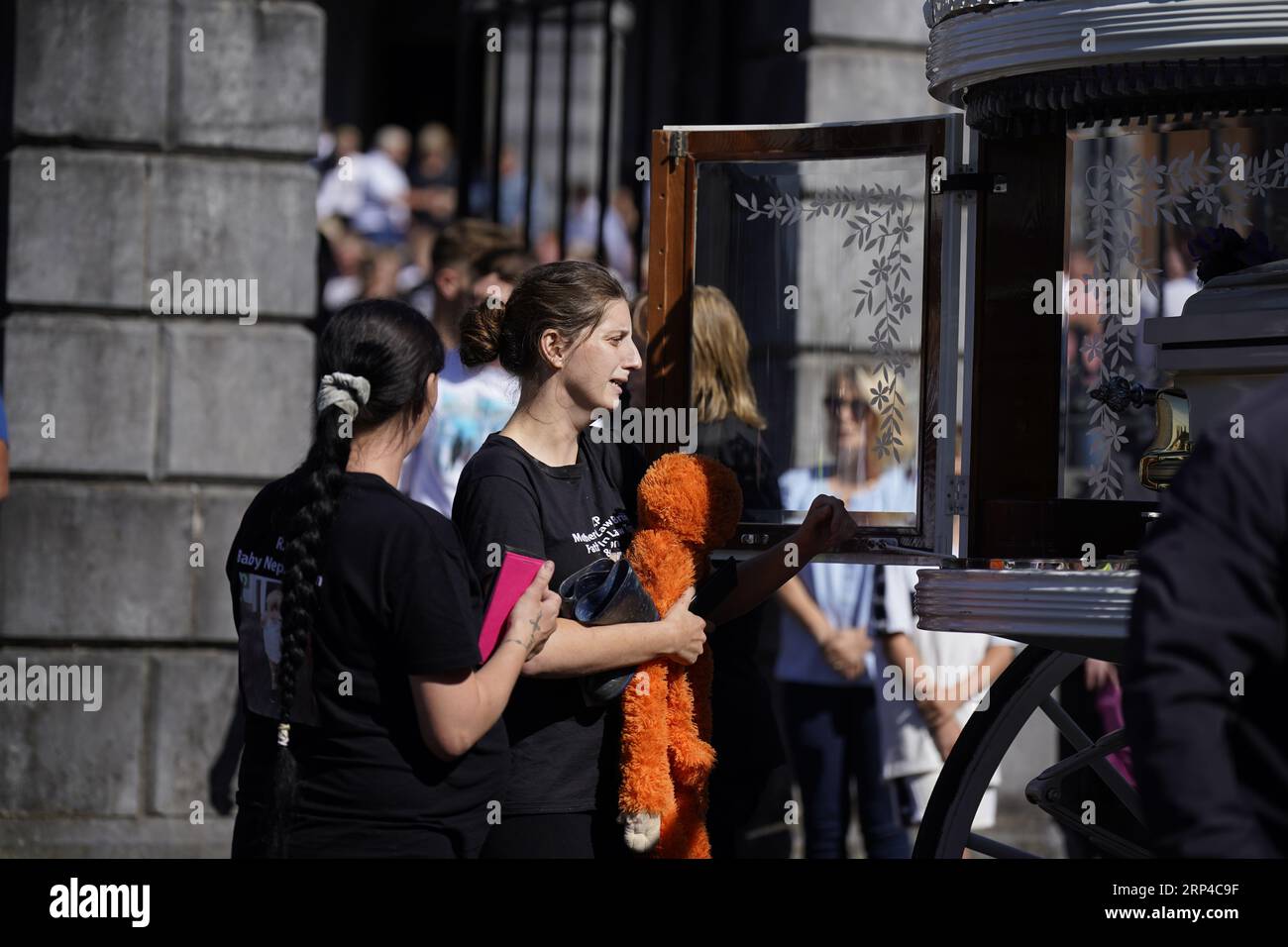 Diane Reilly (carrying orange toy) looks at the coffin of her three ...