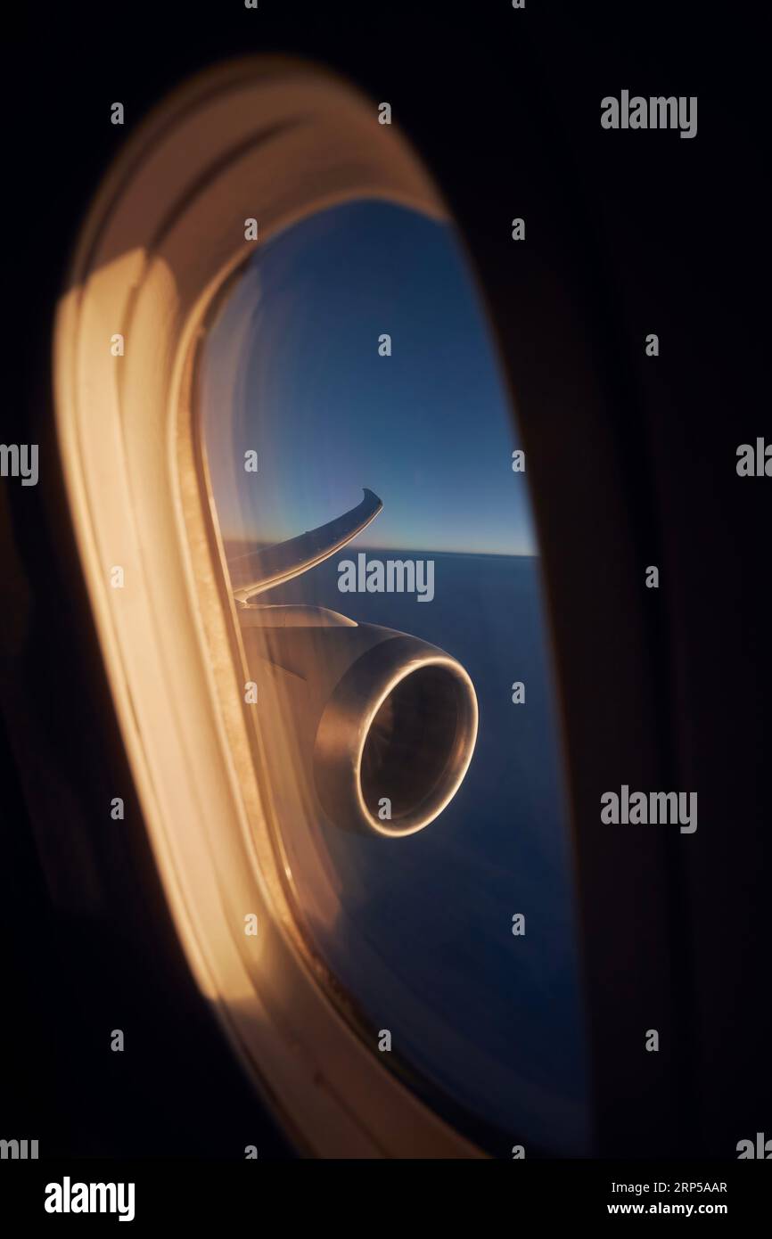 View from airplane window during flight above clouds at dawn. Selective focus on jet engine and ...