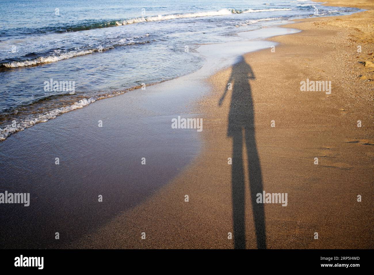 Shadow of a woman standing alone on the beach near the sea at sunset ...
