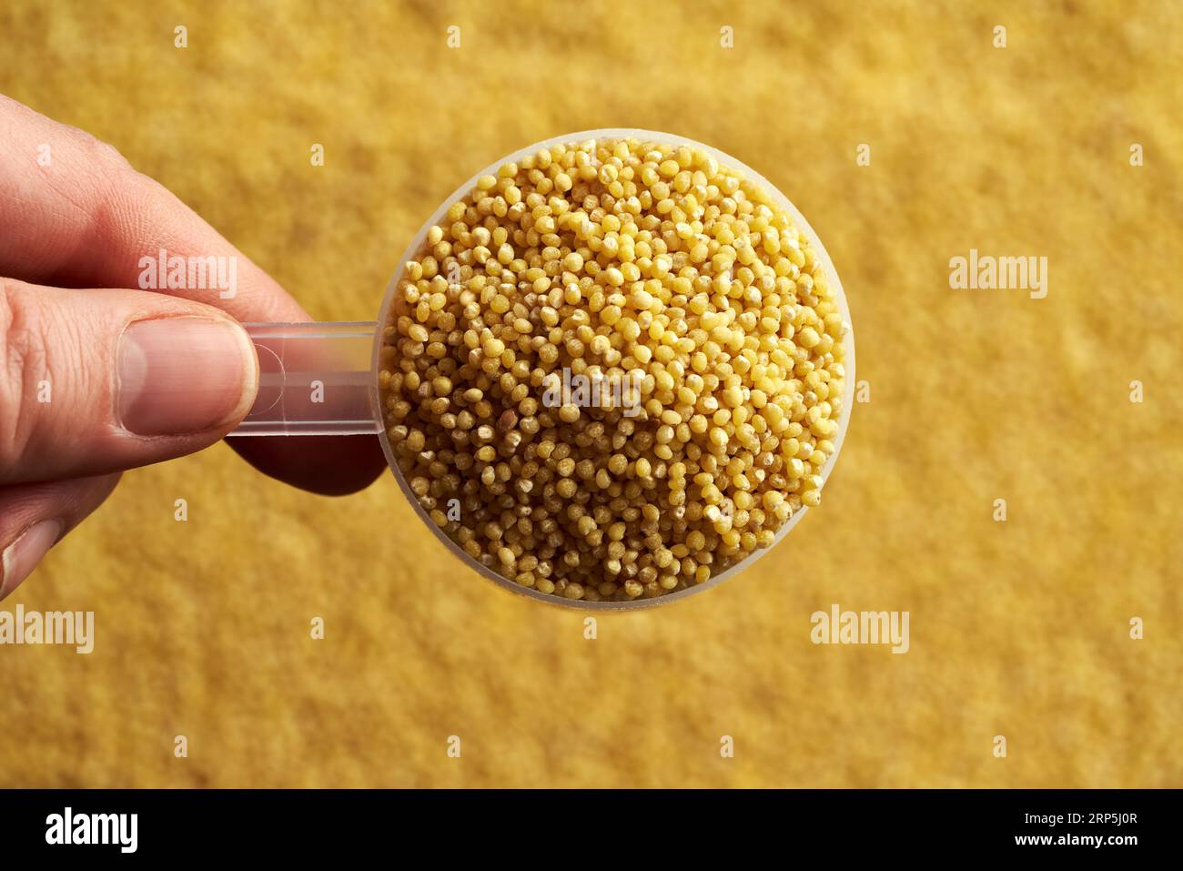 Peeled millet in a plastic measuring cup held by a hand, top view Stock ...