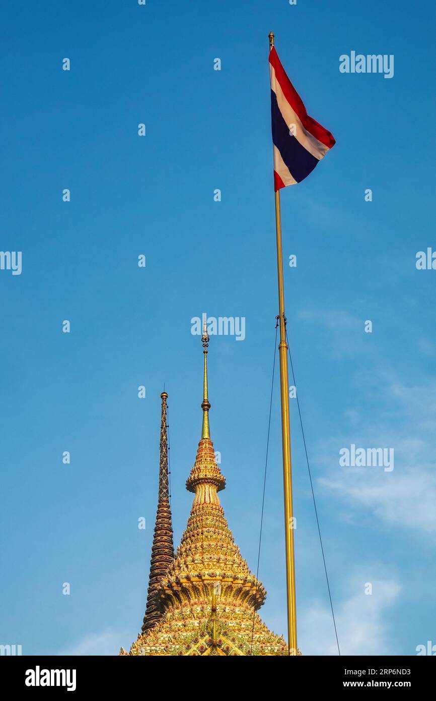 A Thai temple spire and flag against a blue sky. The temple spire is ...