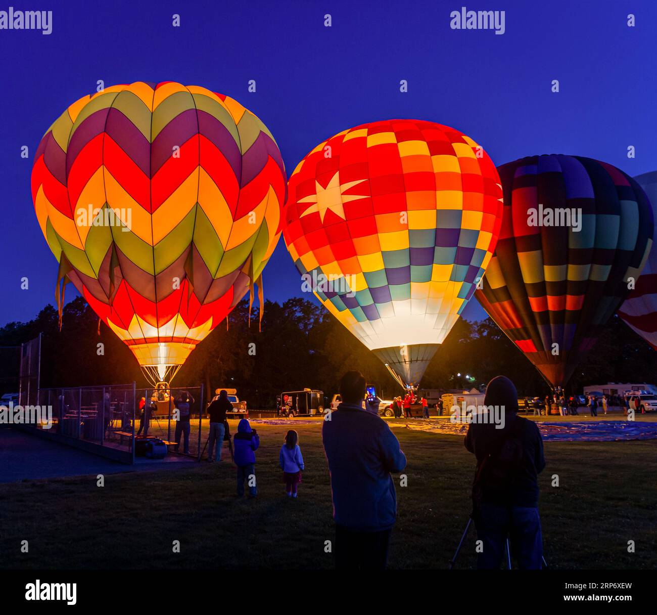 Two hot air balloons are lit up in an early dawn. The gas flame is ...