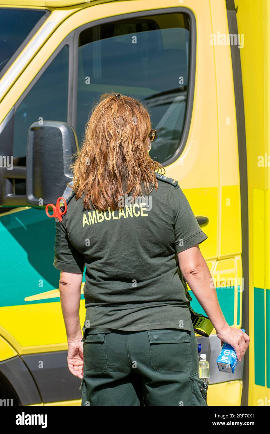 female ambulance worker or paramedic standing next to an emergency ...