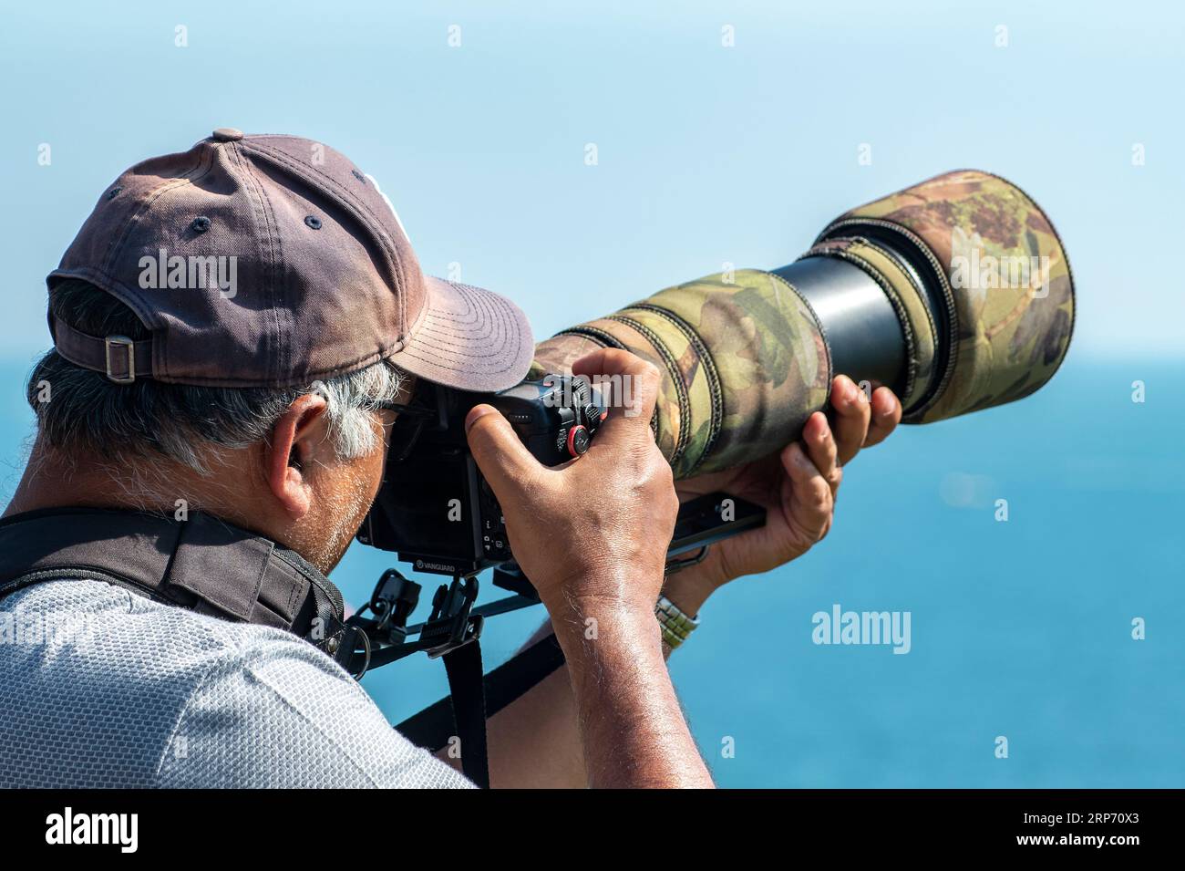 older man wearing baseball cap using a large telephoto lens on a ...