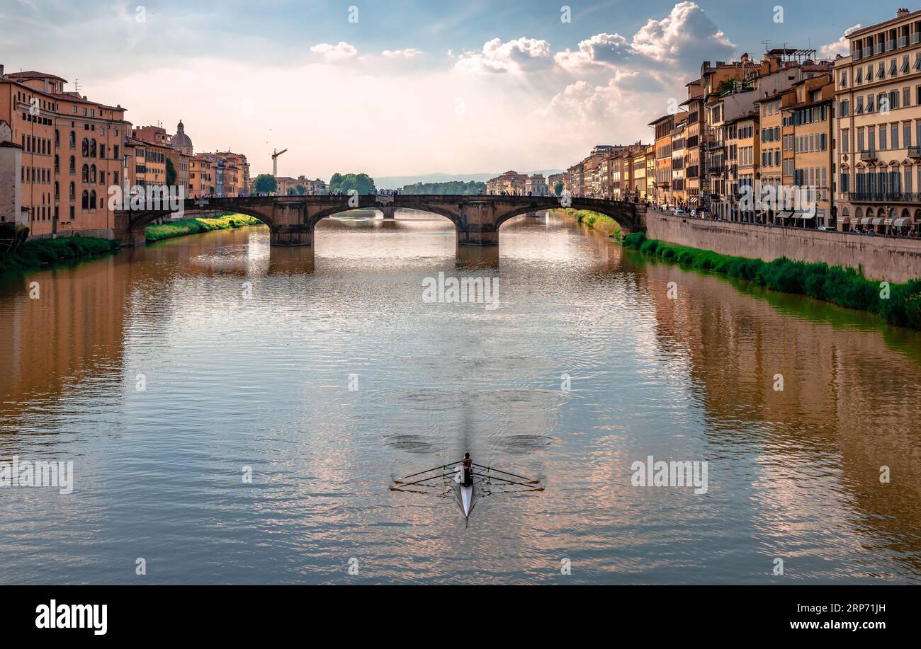 A rowing boat in river Arno, with old medieval buildings in the ...