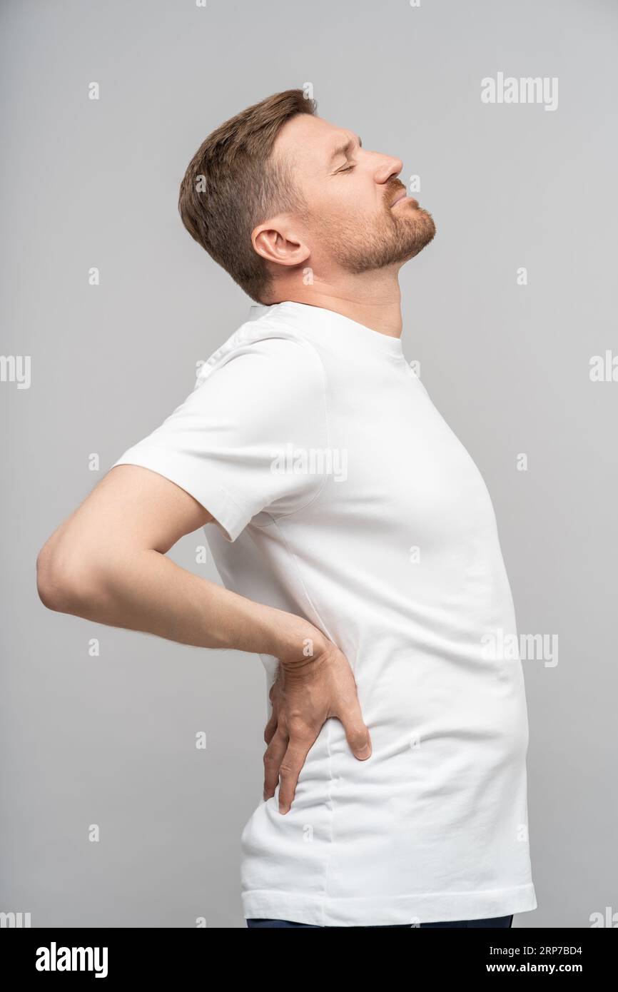 Backache from passive lifestyle. Frowning man touch small of back feels ...