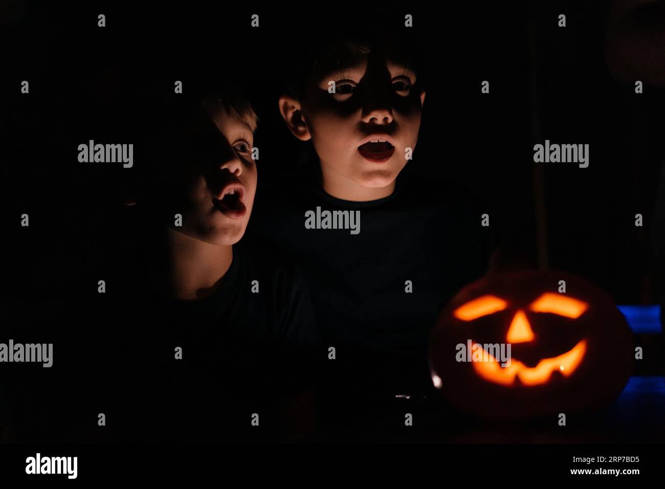 Little boys making scary faces in darkness by light og jack-o-lantern ...