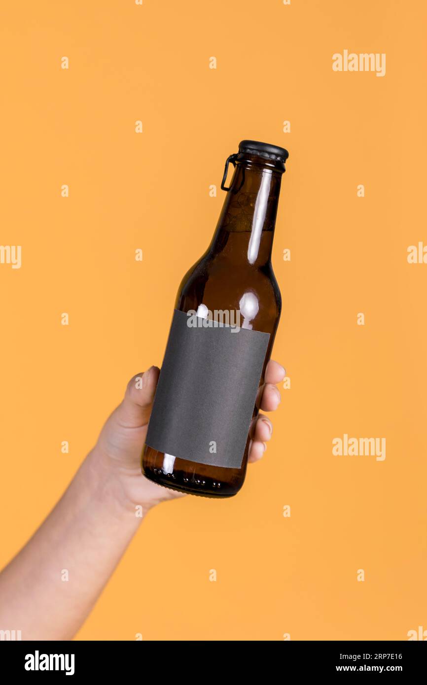 Human hand holding brown beer bottle against yellow wall backdrop Stock ...