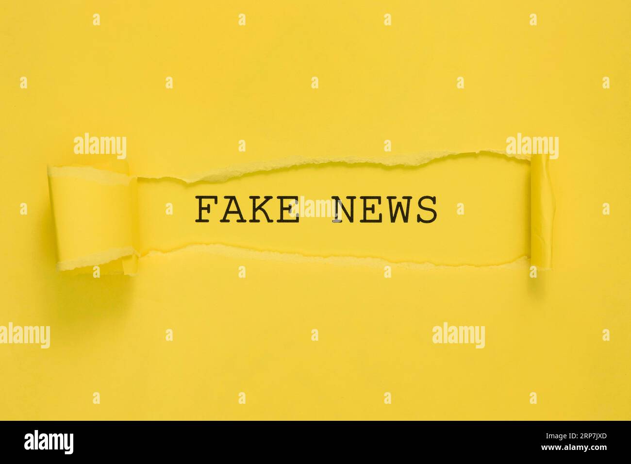 Torn fake news paper yellow wall Stock Photo - Alamy
