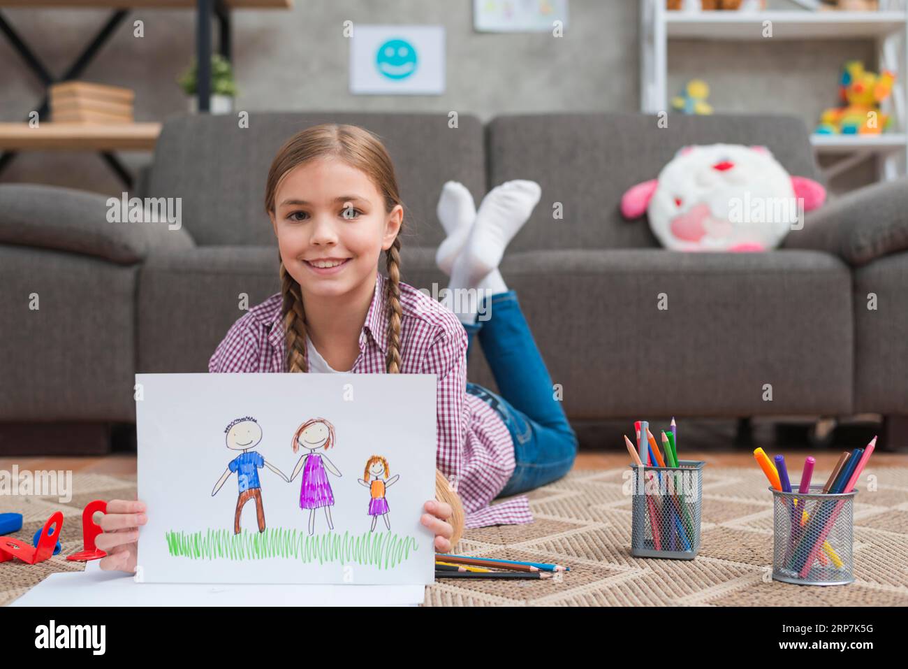 Smiling girl lying carpet showing drawing her family drawn white paper ...