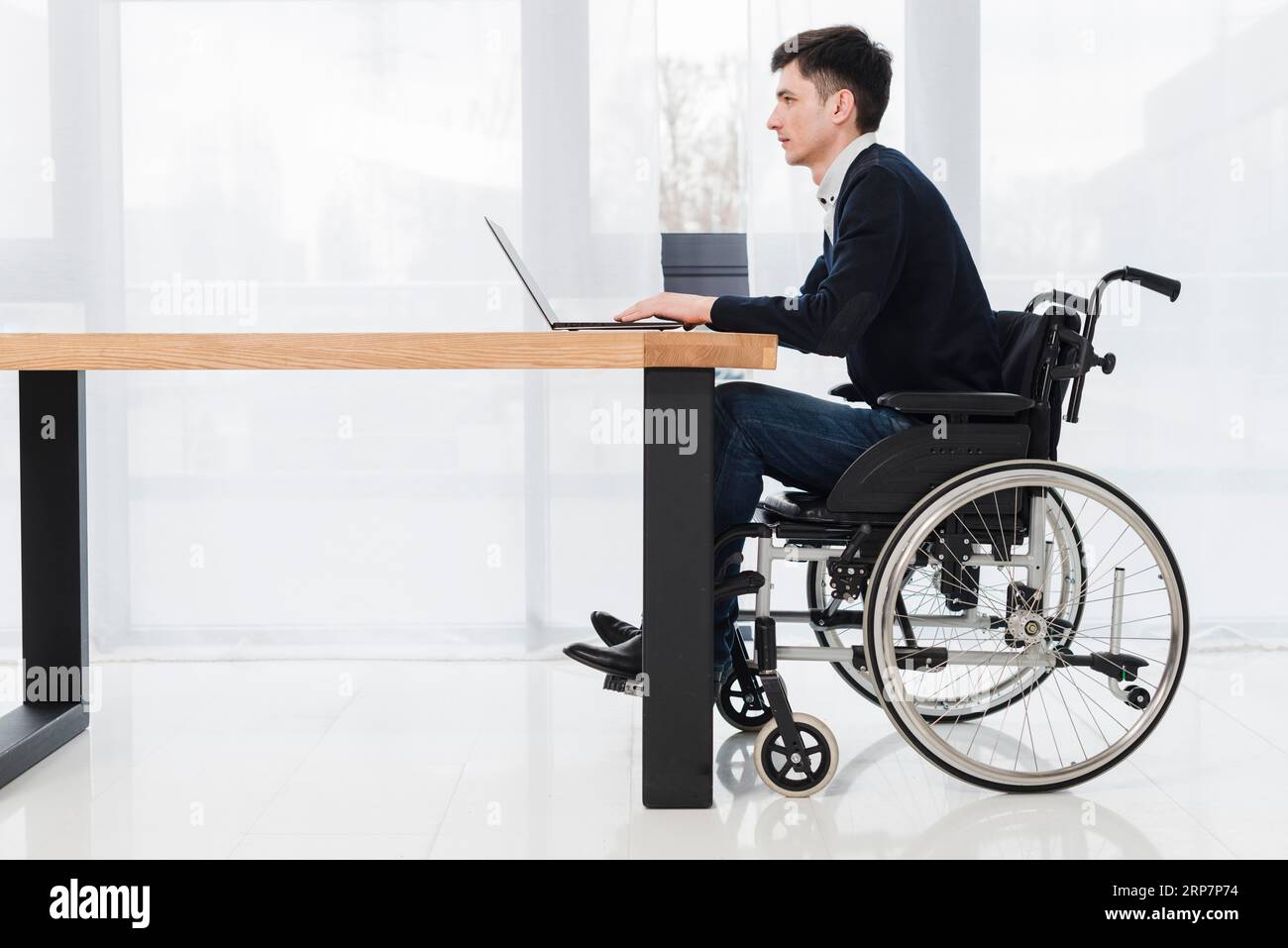 Side view young businessman sitting wheelchair using laptop new office Stock Photo - Alamy