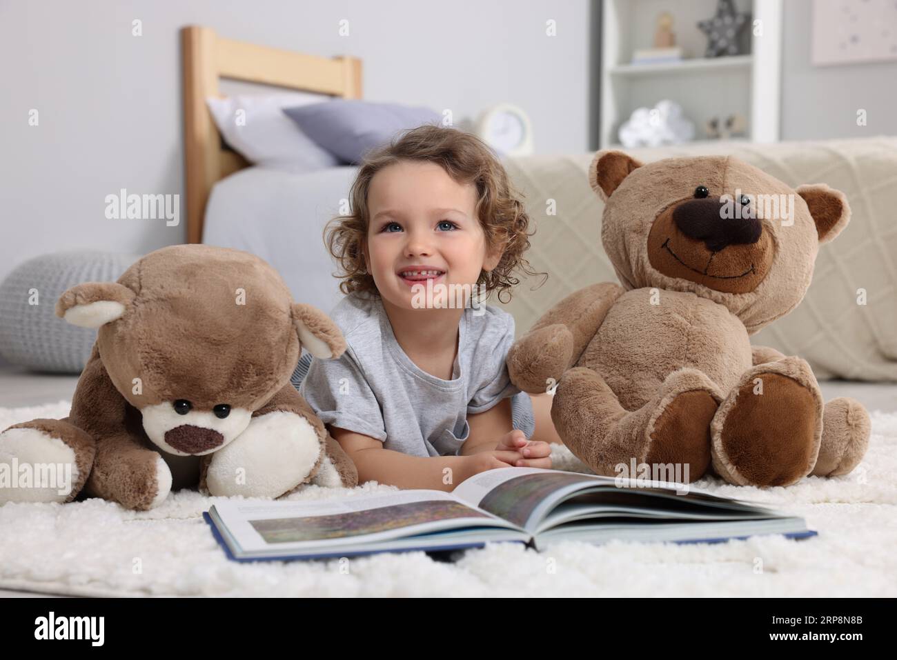 Cute little girl with book and teddy bears on floor at home Stock Photo ...