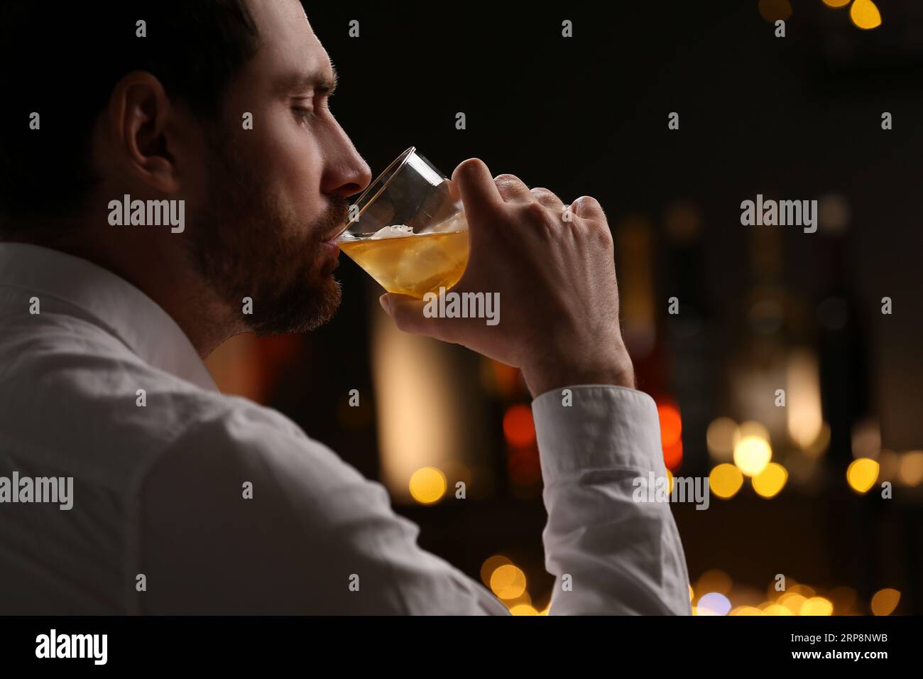Handsome man drinking whiskey against blurred lights Stock Photo - Alamy