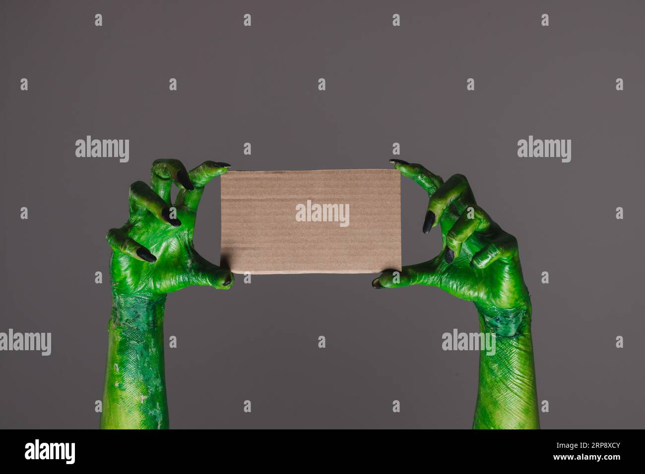 Green monster hands holding cardboard with copy space on grey ...