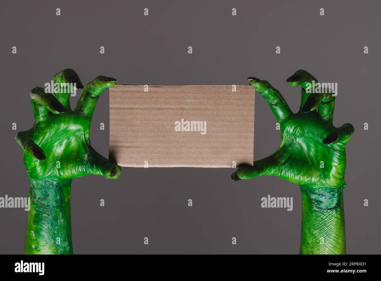 Green monster hands holding cardboard with copy space on grey ...