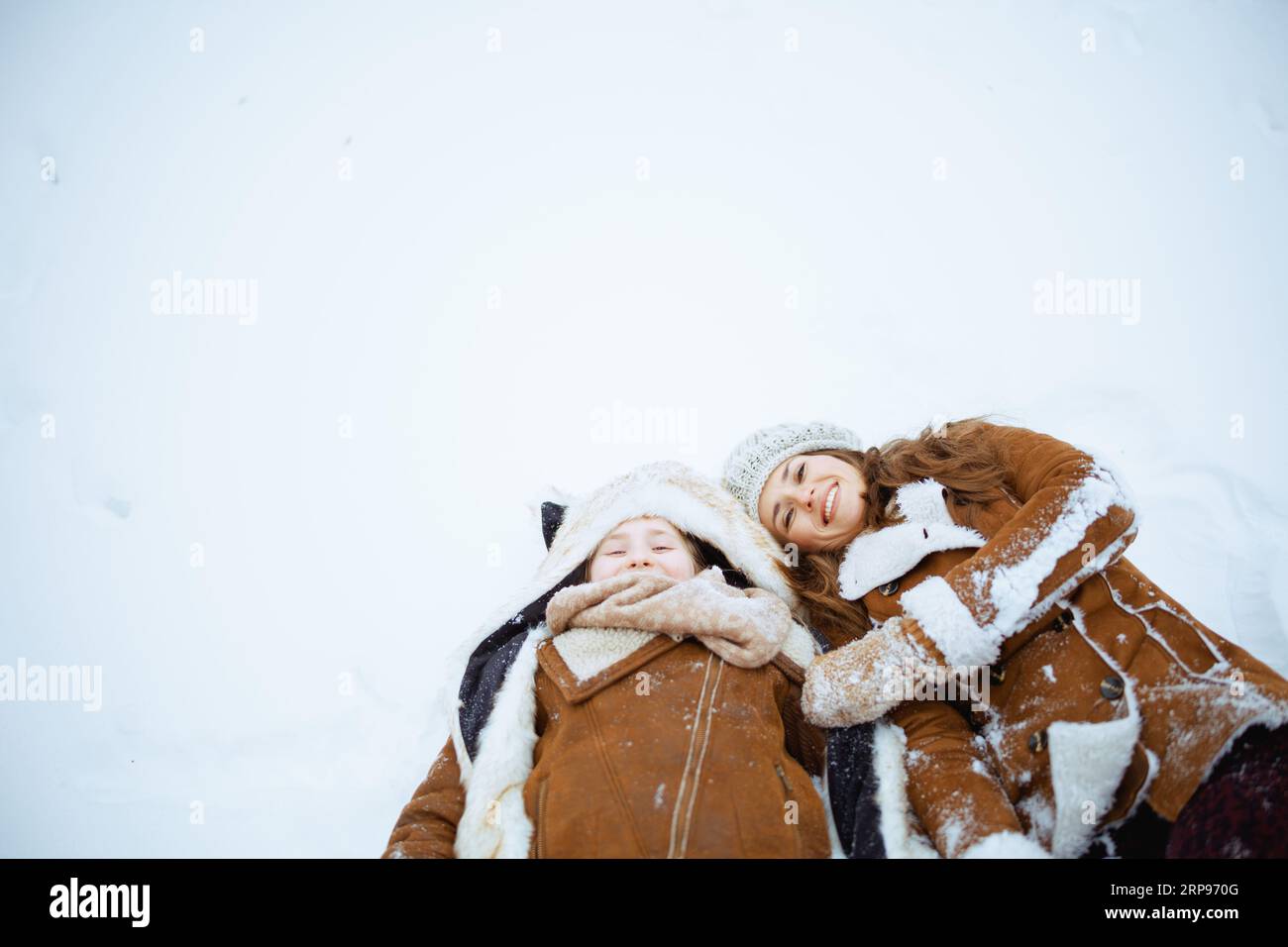 happy modern mother and daughter in coat, hat, scarf and mittens laying ...
