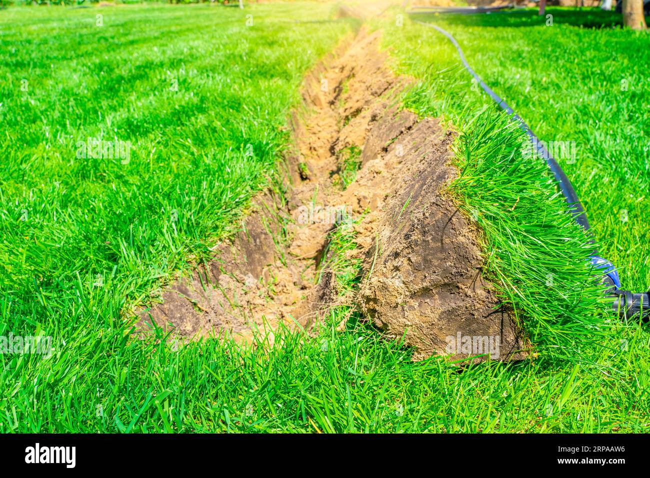 A ditch dug in the lawn for laying pipes and installing irrigation ...