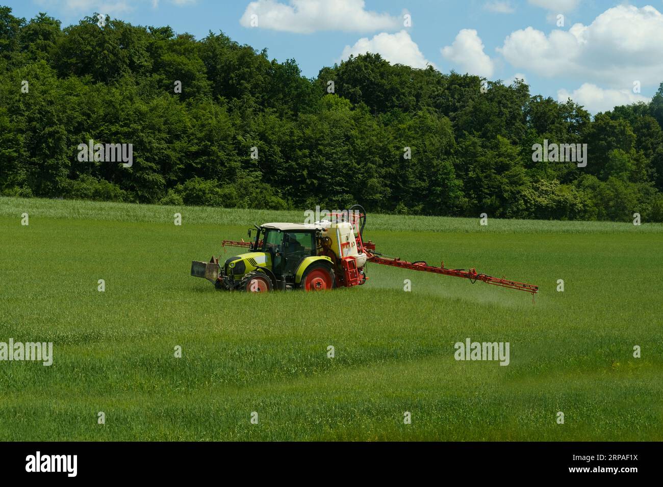 A farmer sprays fertilizer through a sprayer while riding in a tractor ...