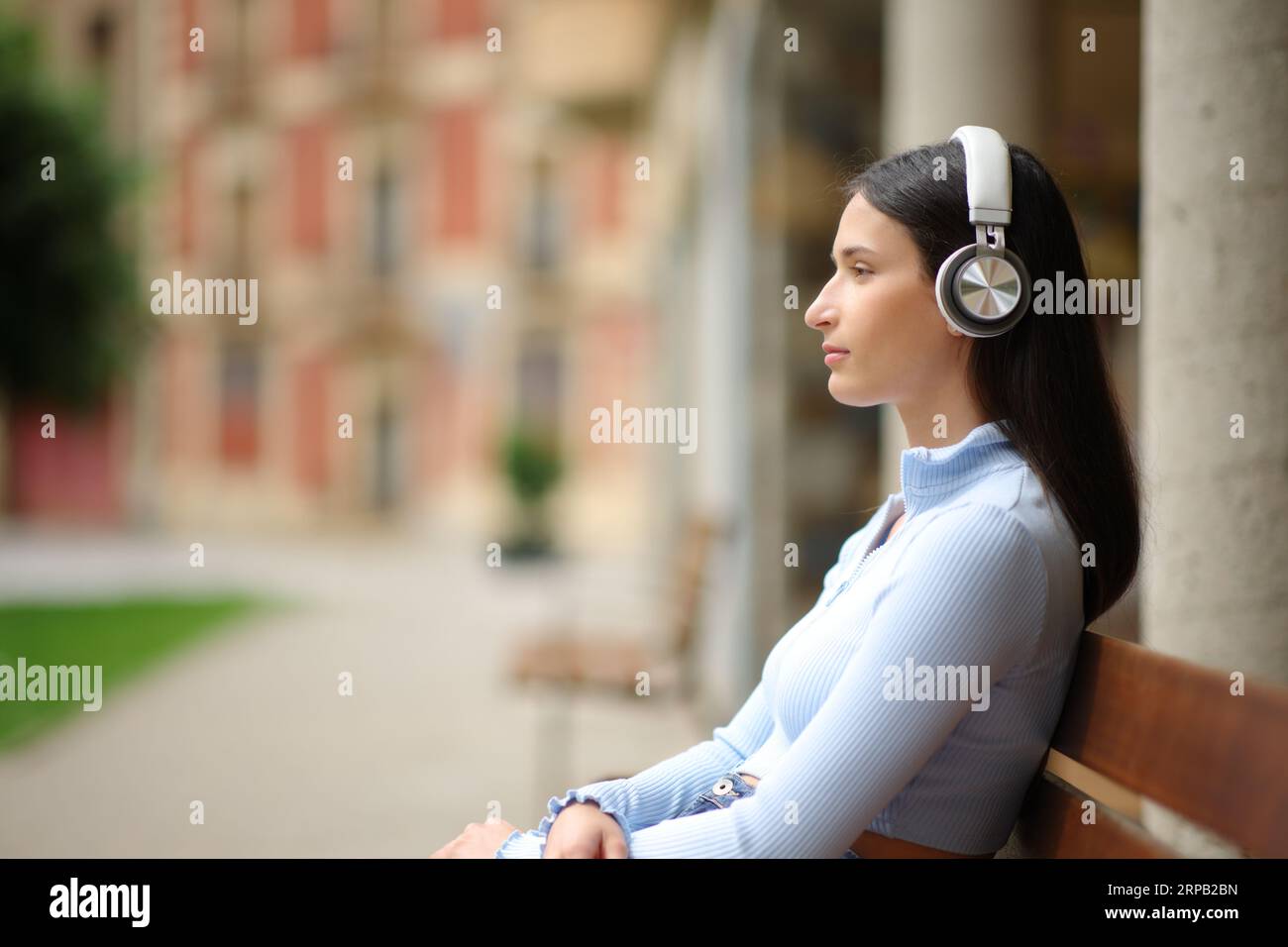 Side view portrait of a serious woman sitting in a bench listening to ...