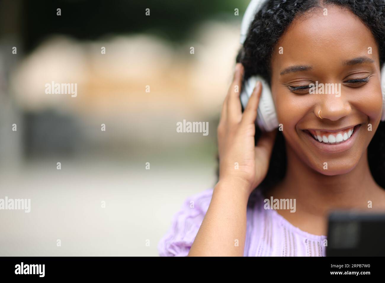 Front view portrait of a happy black woman listening audio on phone in ...