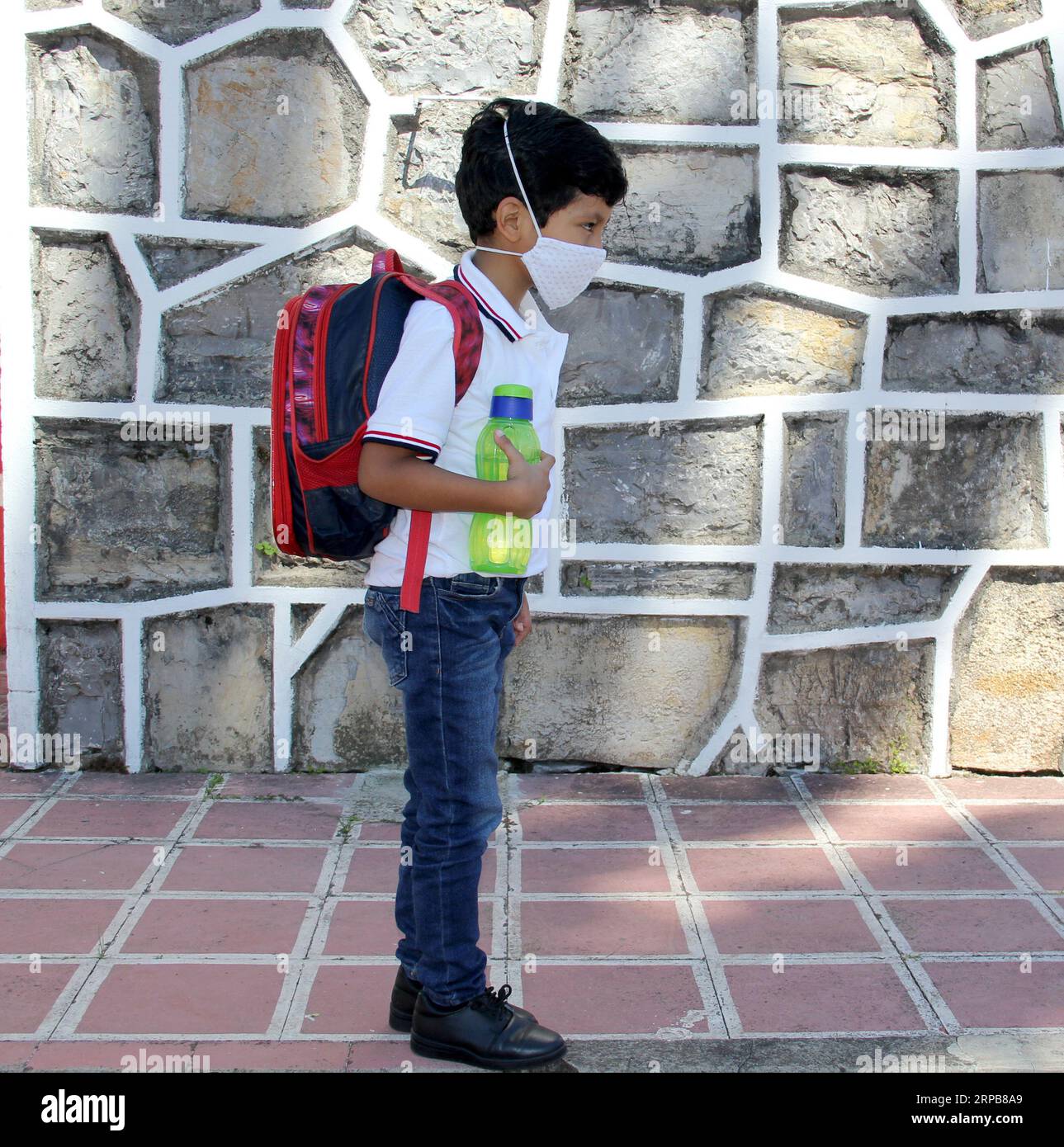 Latino boy with uniform shirt, mask, backpack, notebook and bottle of ...