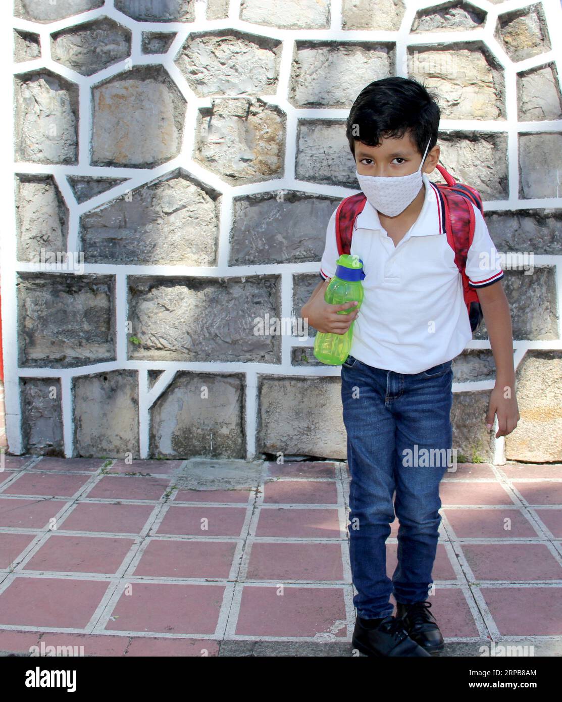 Latino boy with uniform shirt, mask, backpack, notebook and bottle of ...