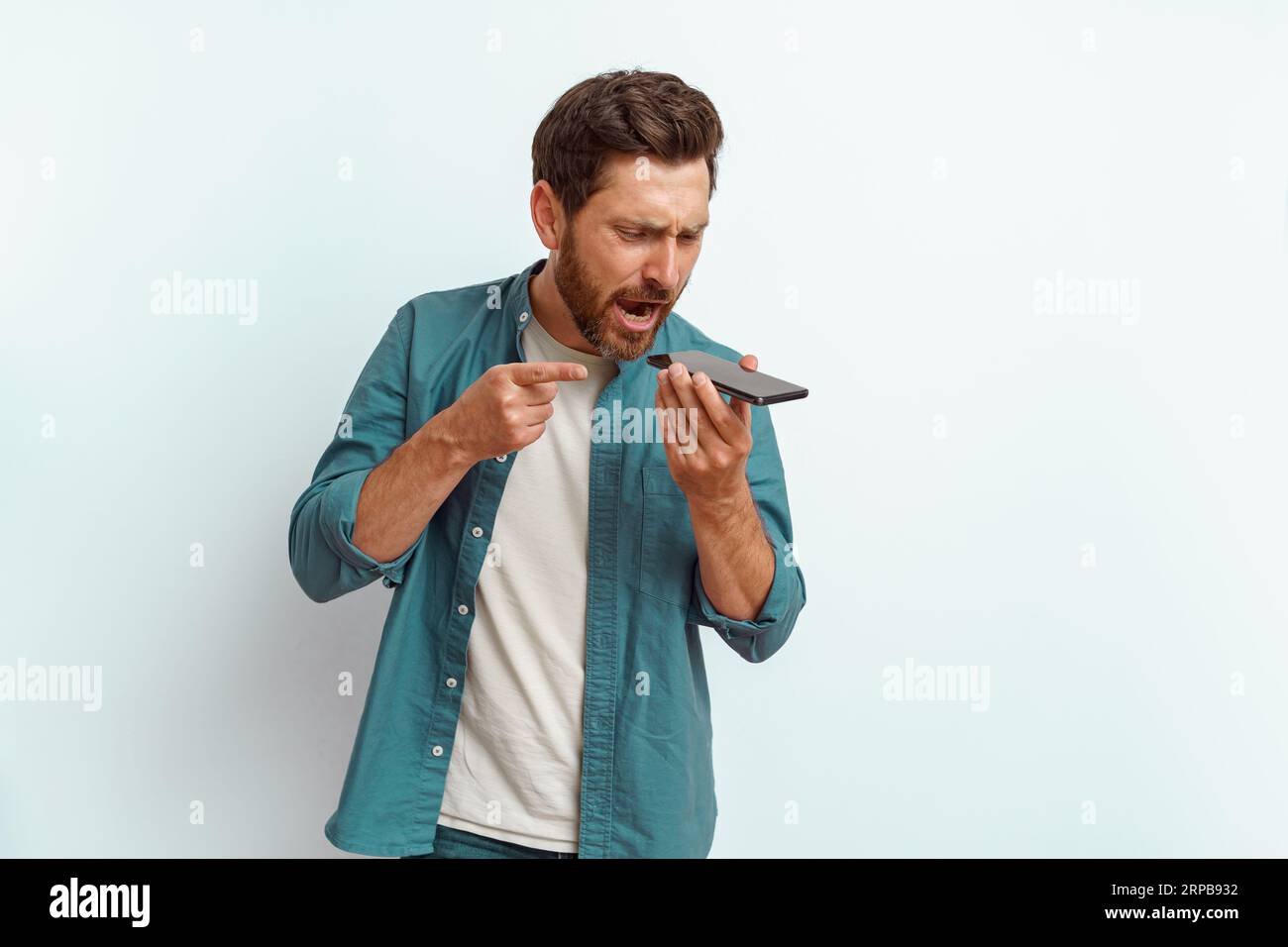 Angry man shouting and recording audio message on phone while standing ...