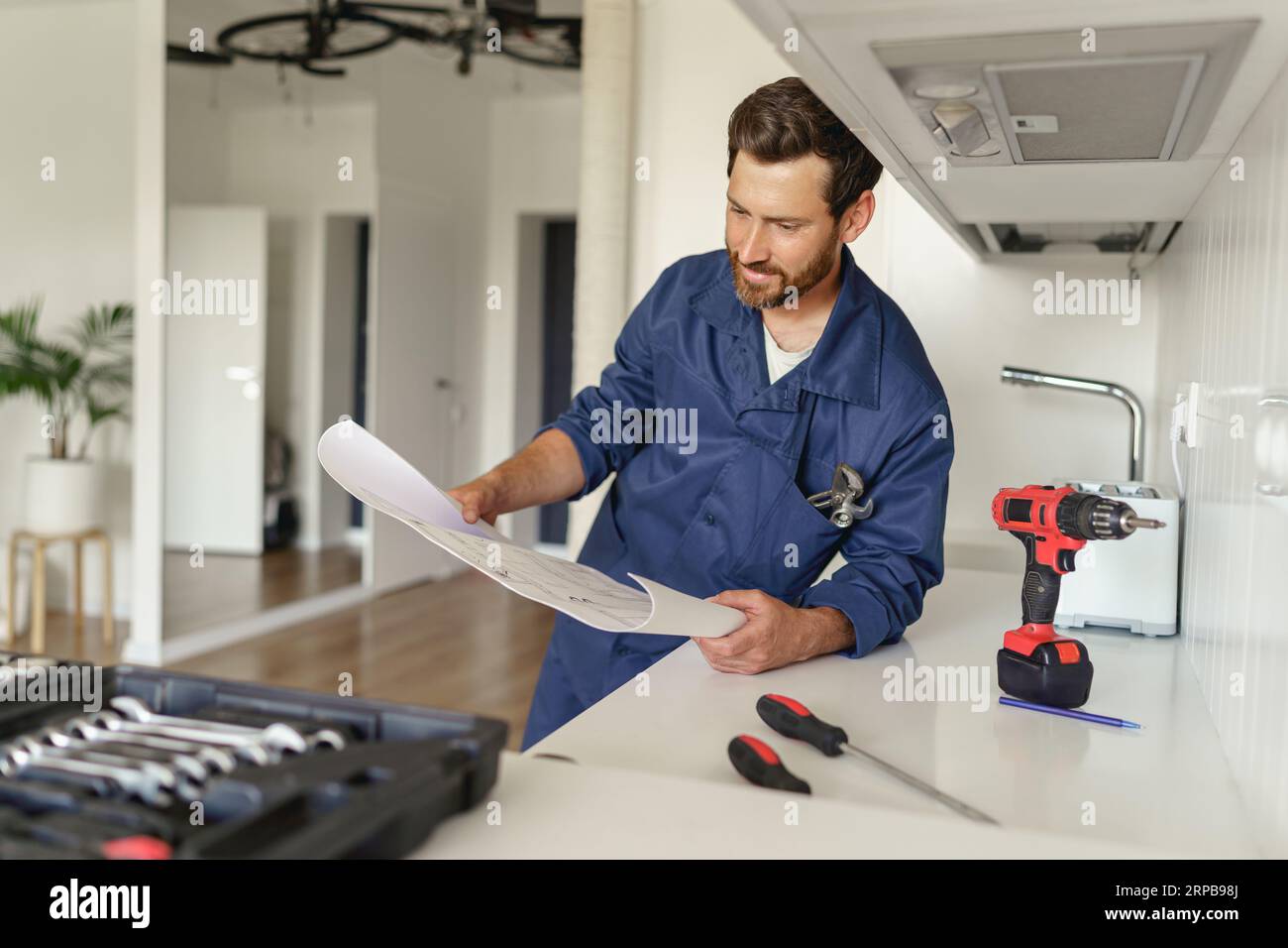 Handyman in uniform standing on kitchen with home plan and tool box ...